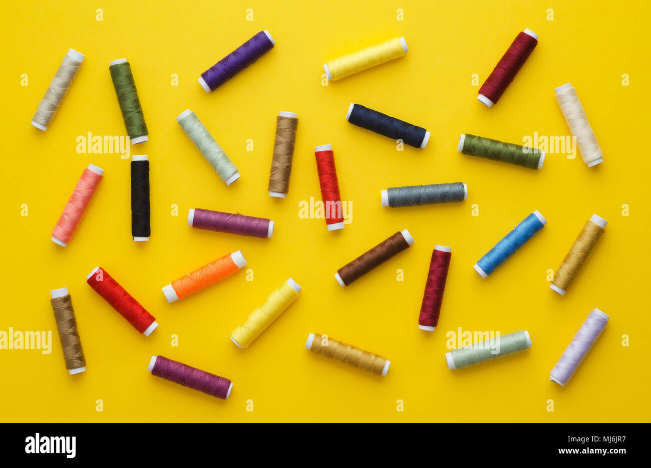 Colorful thread spools disorganized over bright yellow background ...