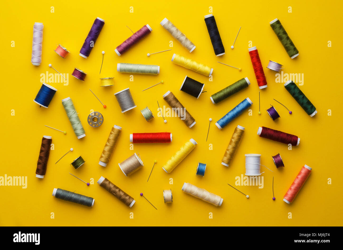 Colorful thread spools disorganized over bright yellow background ...