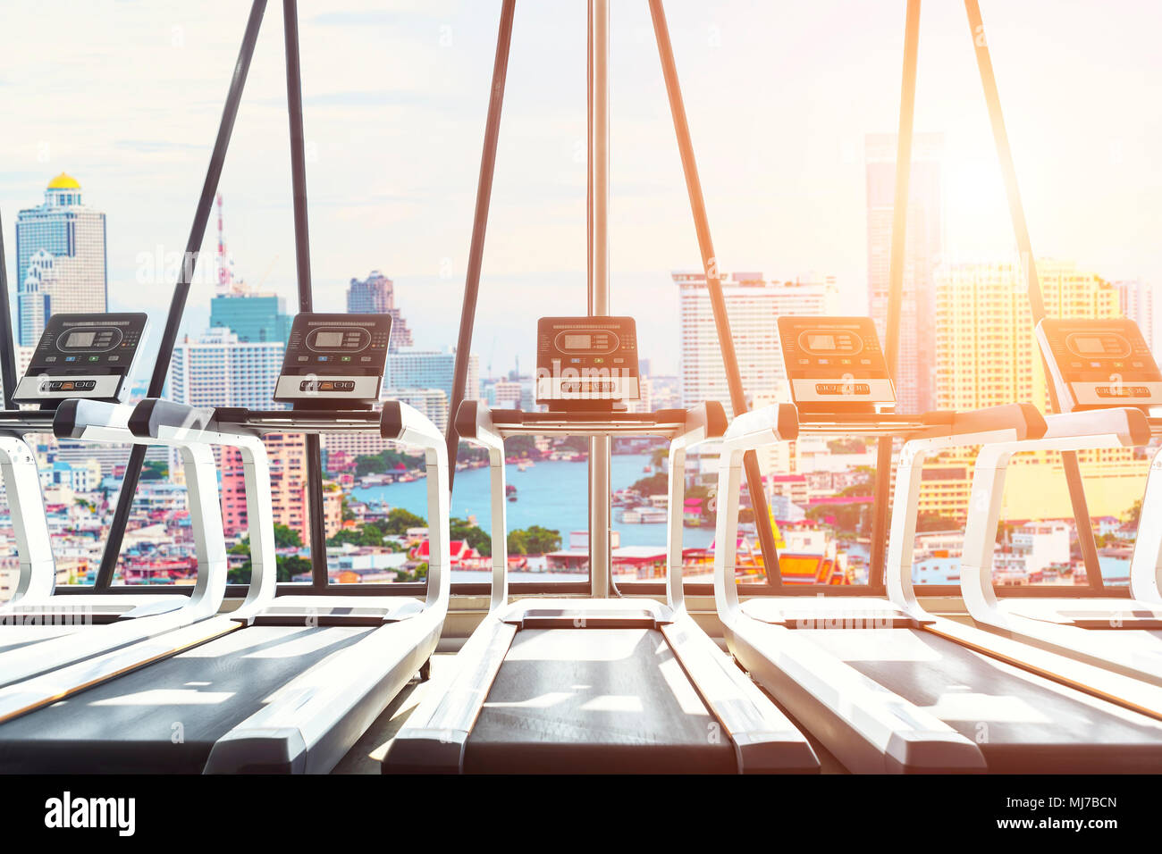 Interior of modern treadmills in gym at sunrise with view of city ...