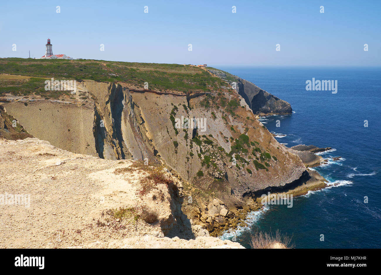The view of a big limestone cliffs over Praia do Cavalo or Horses beach and a lighthouse on the ...