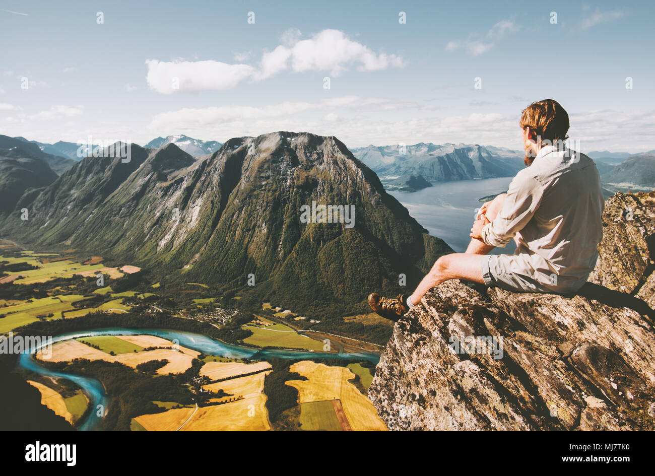 Man sitting on cliff edge relaxing with aerial mountains landscape Travel lifestyle adventure ...