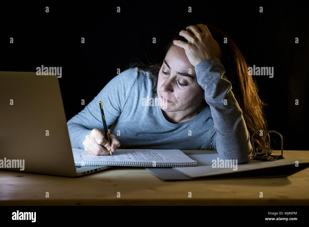 Overworked and tired female student working last at night on her laptop ...