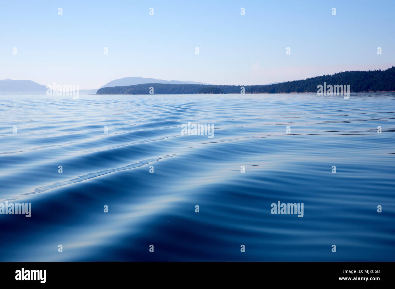 Surface view of ocean with gentle waves, mountains in the distance ...