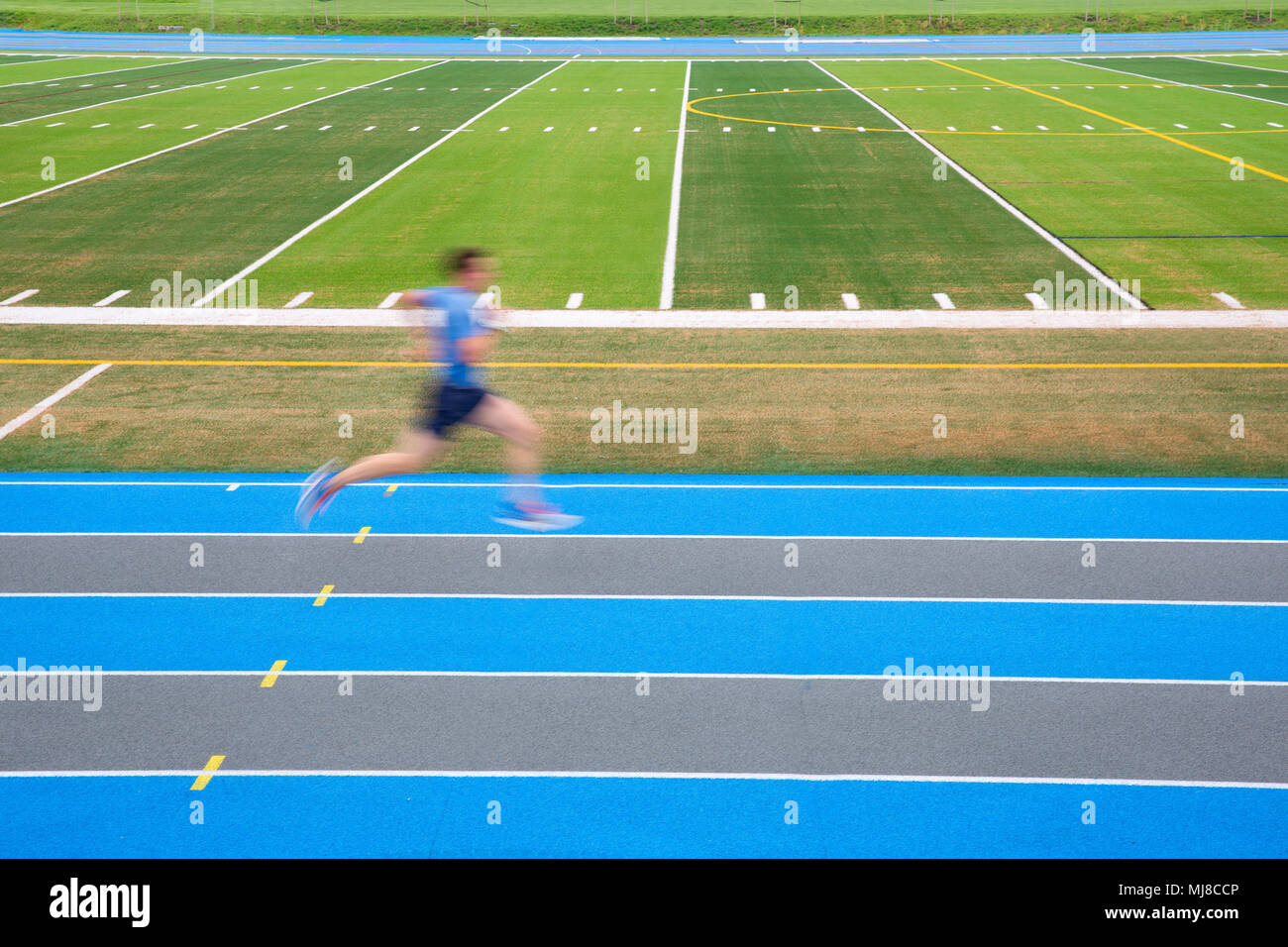 Side view of man running on blue track on sports field, motion blur ...