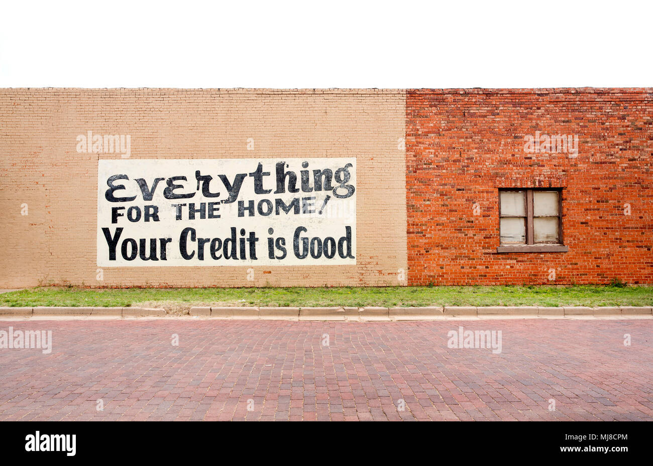 Old advertisement on painted brick wall, grass verge and cobbled street ...