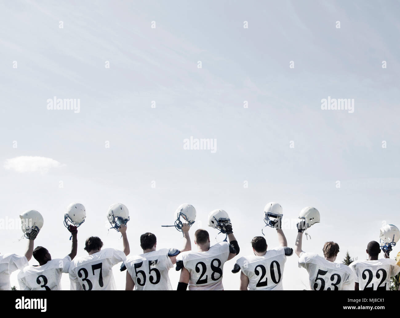 Rear view of football team standing side by side, holding aloft helmets ...