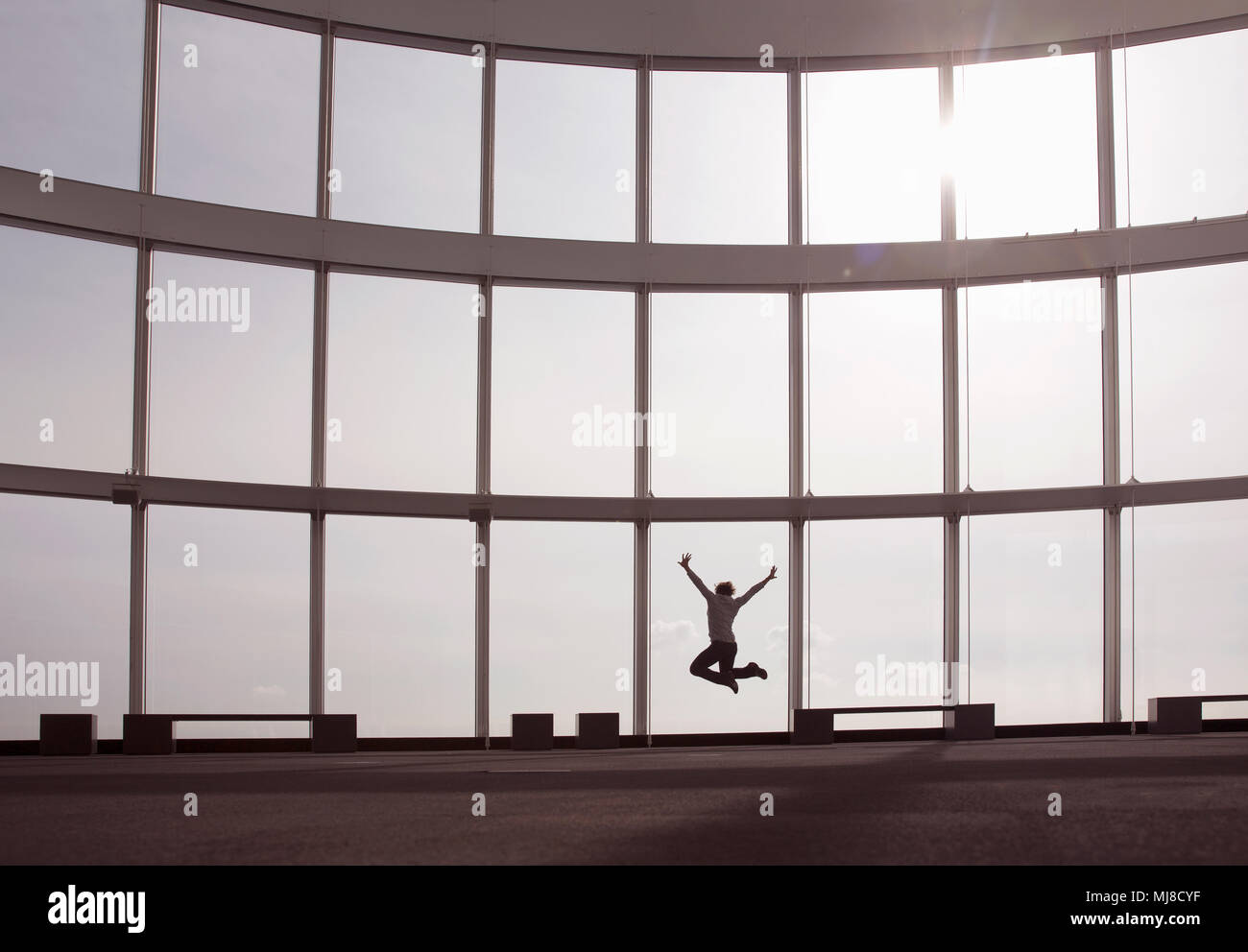 Rear view of person jumping in the air in front of tall glass wall ...