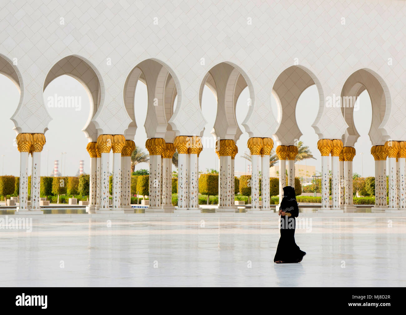 Woman walking past colonnade of mosque with white washed and golden ...