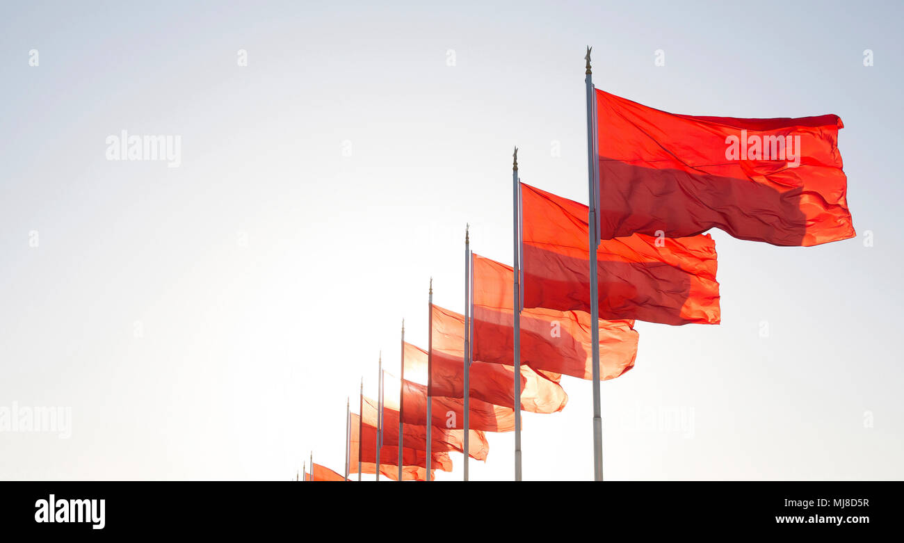 Row of bright red flags on flagpoles fluttering in the wind, clear sky ...