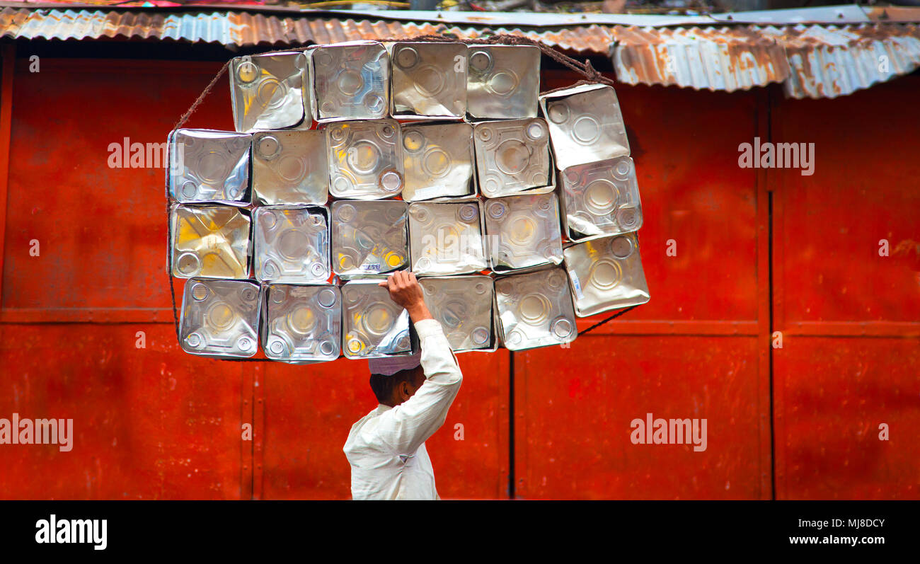Side view of man carrying stack of metal containers on his head ...