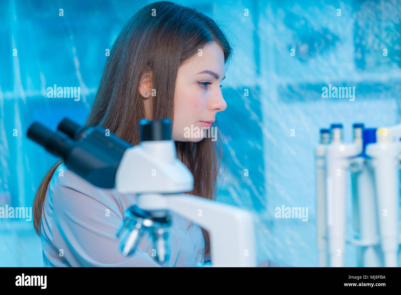 Young pretty girl student peering through microscope in science ...