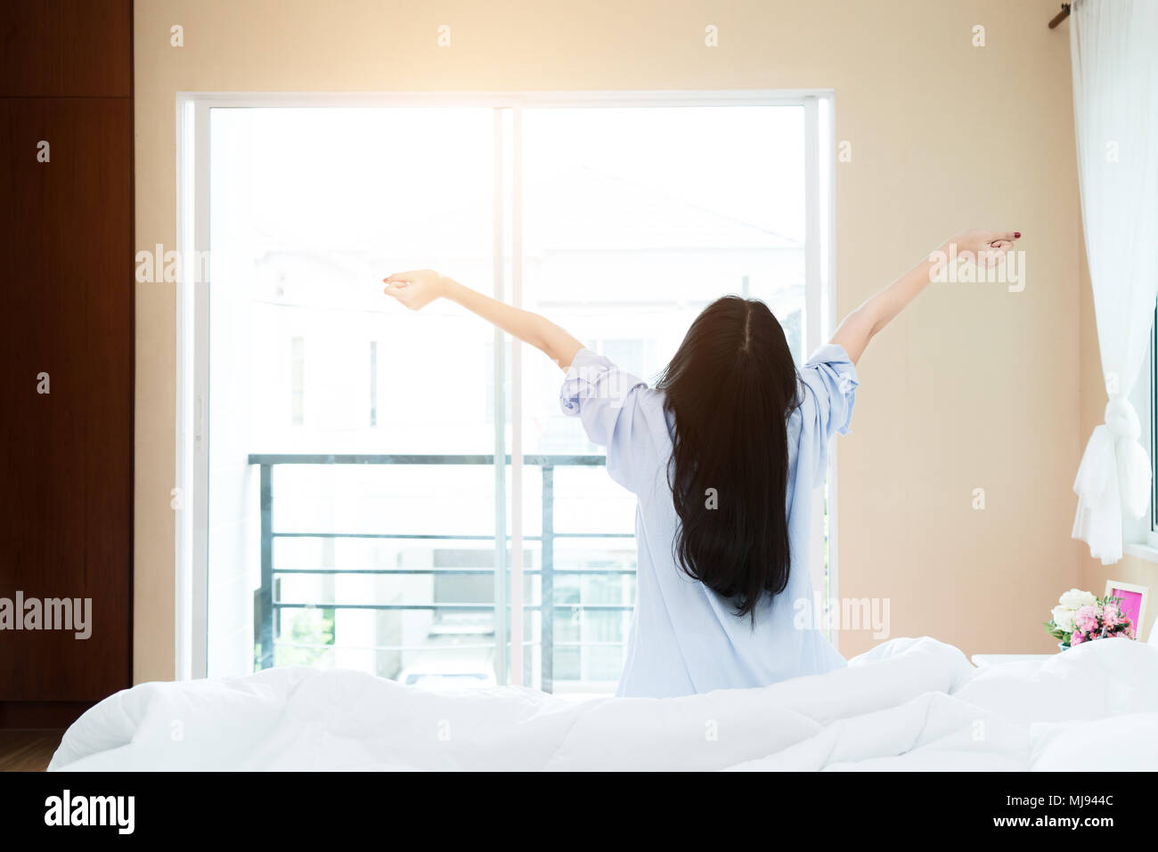 Back view of Asian woman stretching in bed after wake up, rising hands ...