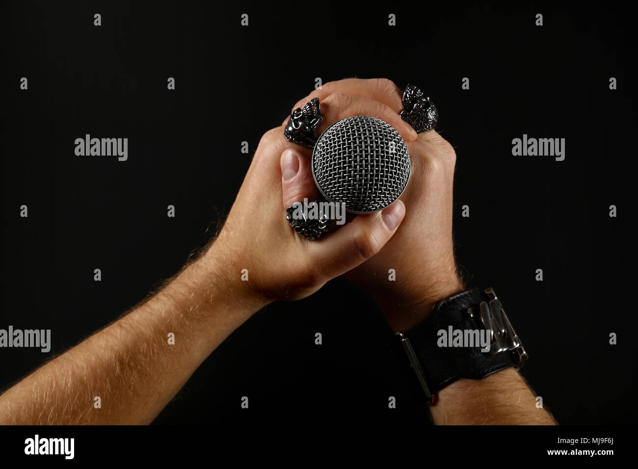 Close up man two hands with metal rings and bracelet holding microphone ...