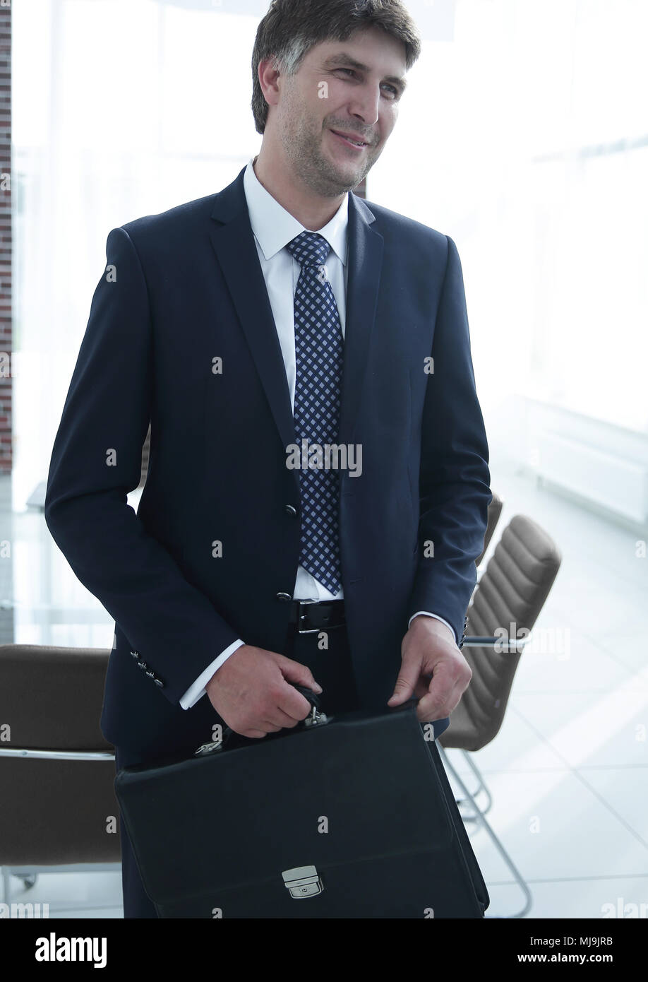 Business man with briefcase standing on office background Stock Photo ...