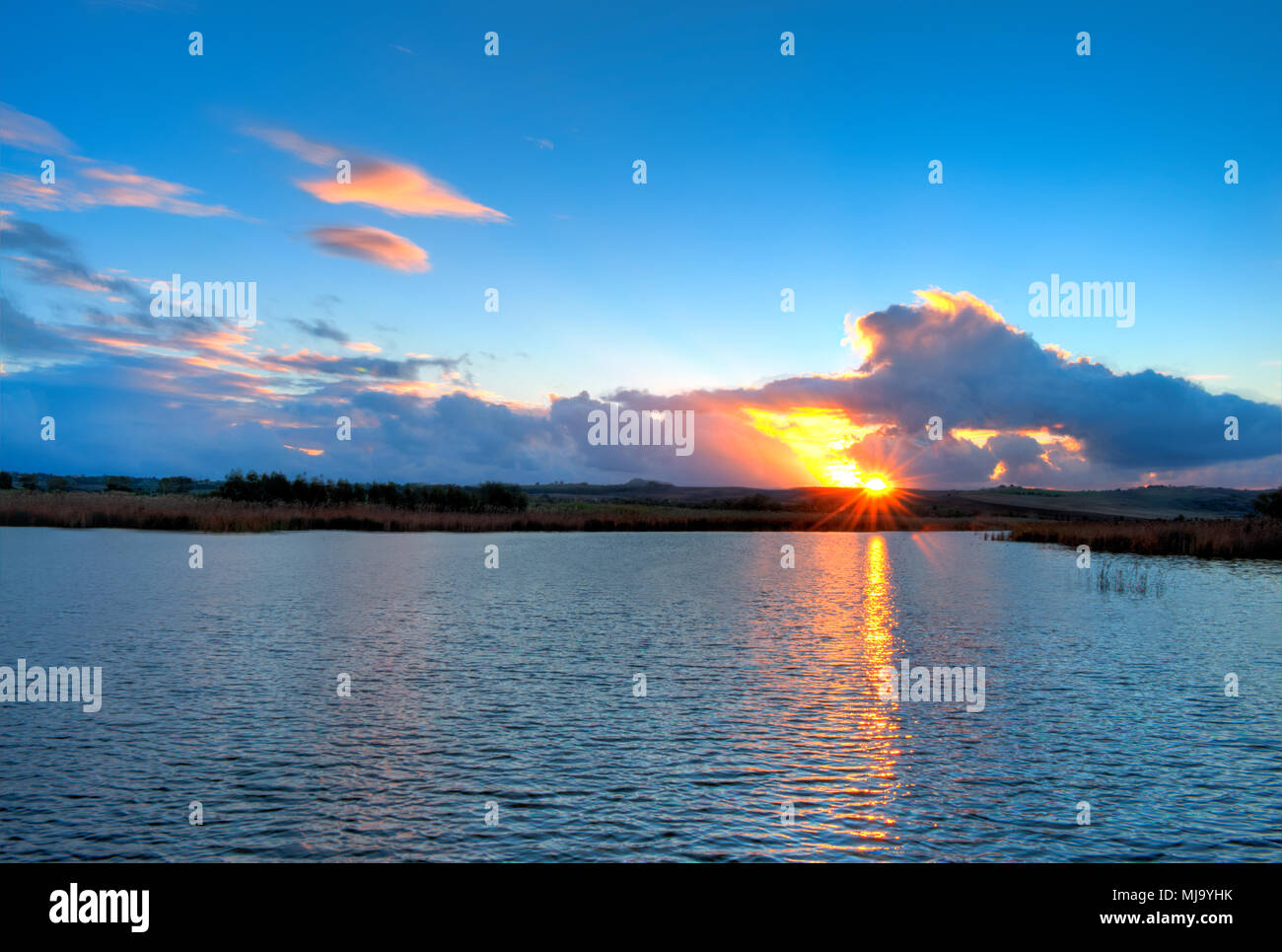 Landscape of pond at sunset with sun behind the clouds Stock Photo - Alamy