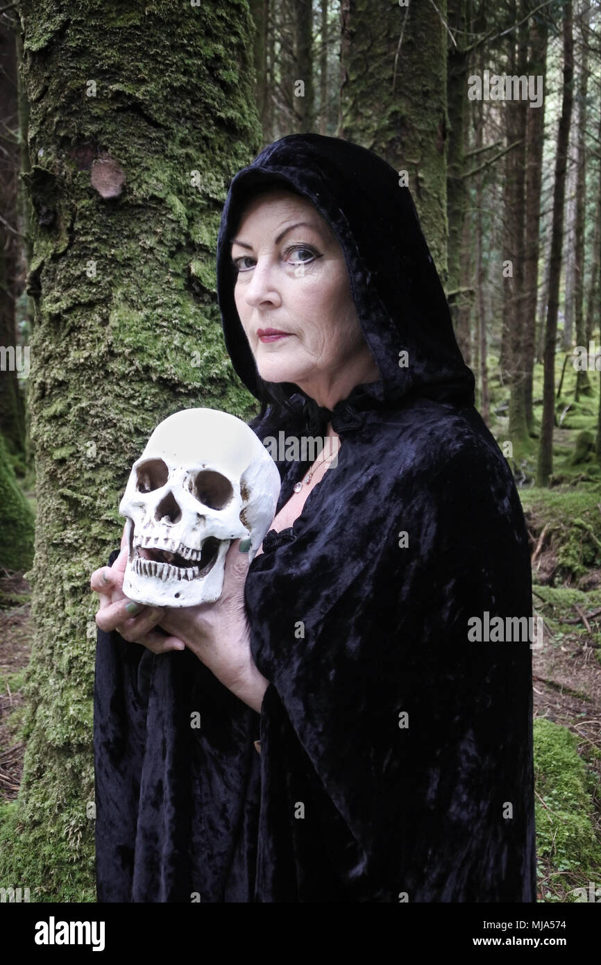 A female witch holding a human skull in dark woods - John Gollop Stock ...
