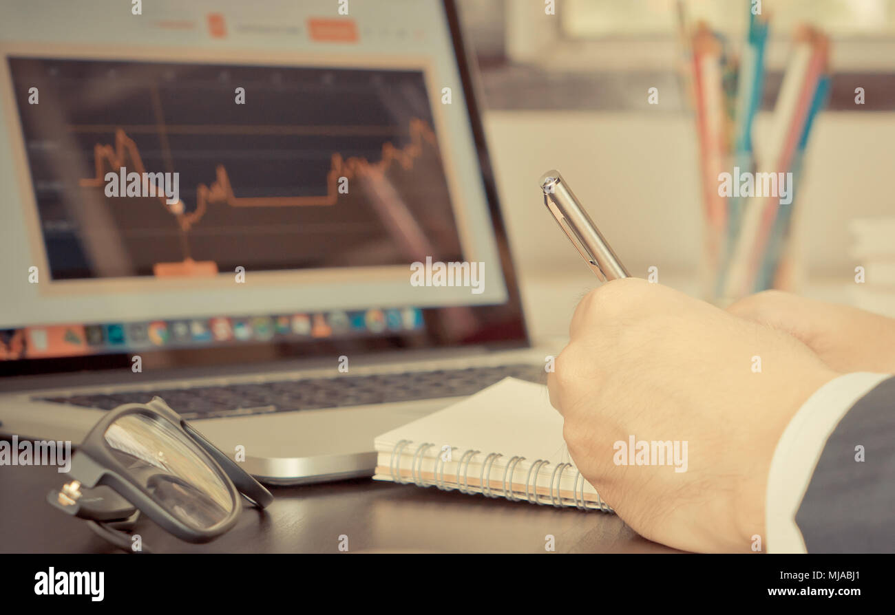 Stock Market broker is taking note on Stock analysis on computer screen ...