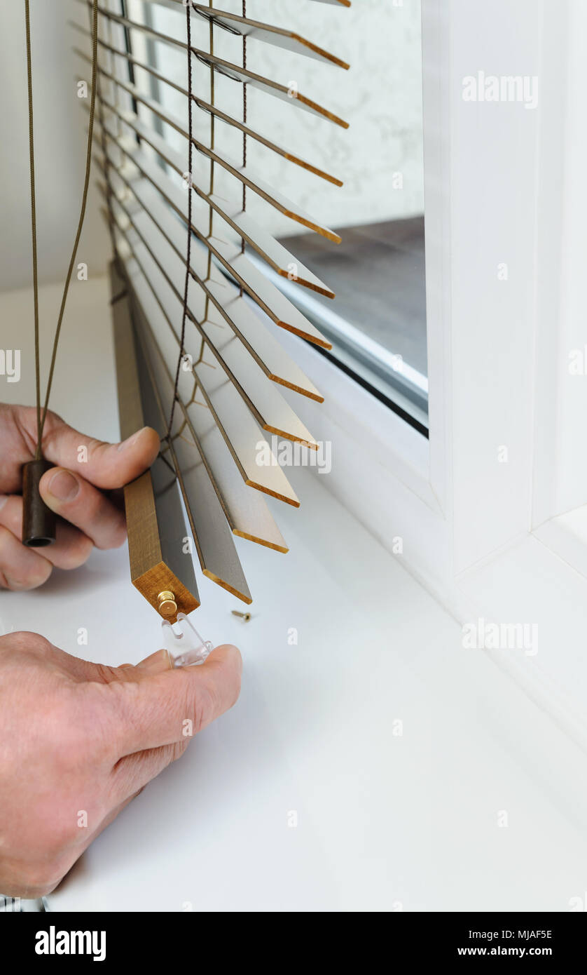 Installing wooden blinds. Man attaches the plastic braket to the bottom ...