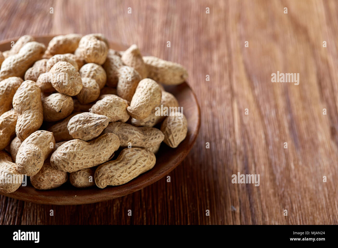 Unpeeled peanuts in wooden bowl over rustic wooden background closeup ...