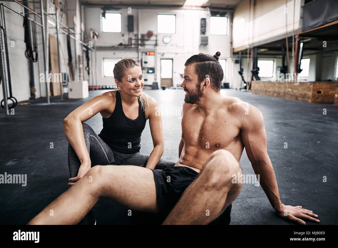 Two fit young people in sportswear sitting together on a gym floor ...