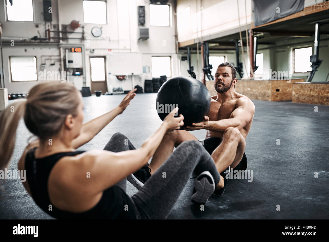 Two fit young people in sportswear sitting together on a gym floor ...