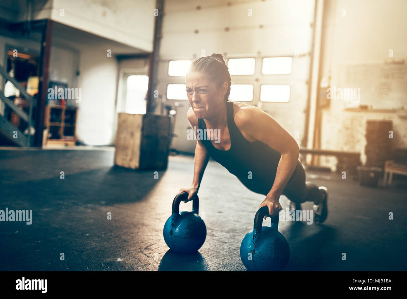Fit young woman straining to do pushups on dumbbells while working out ...