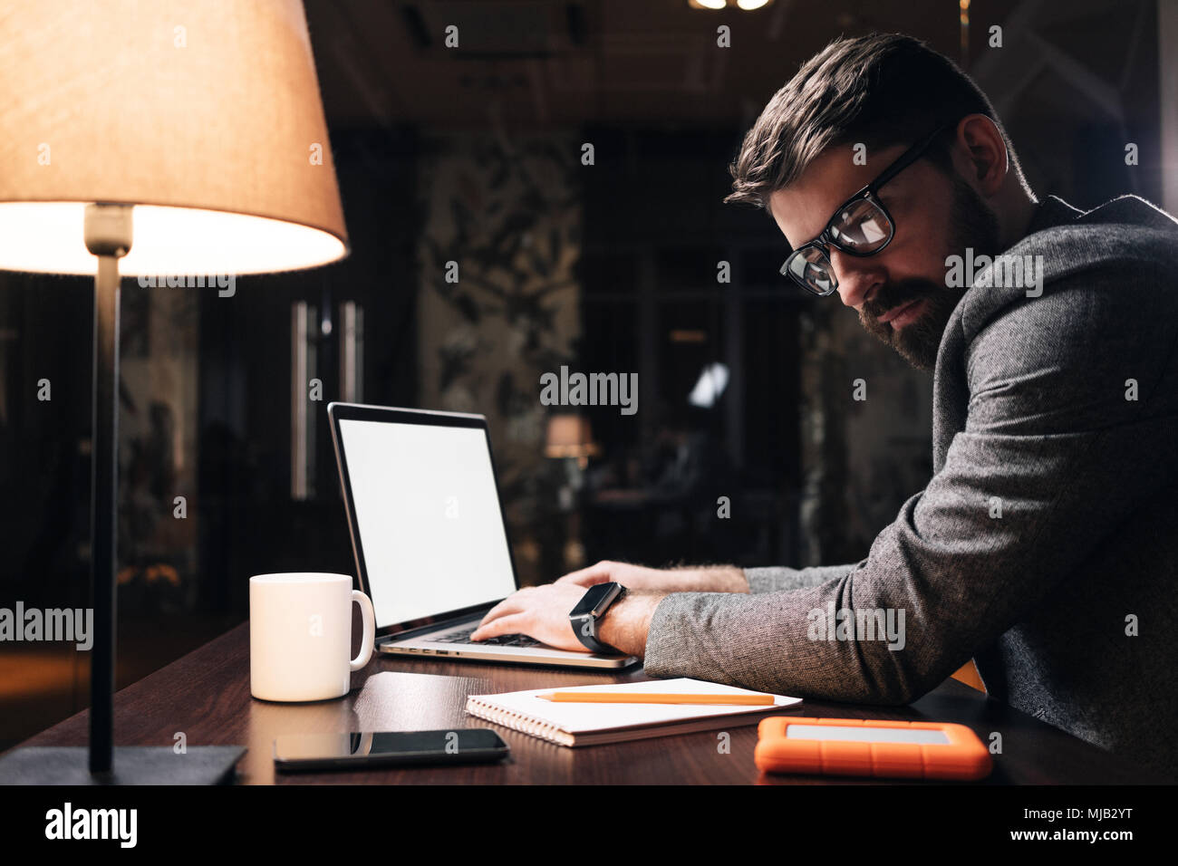 Young project manager typing text on laptop at night office. Bearded ...