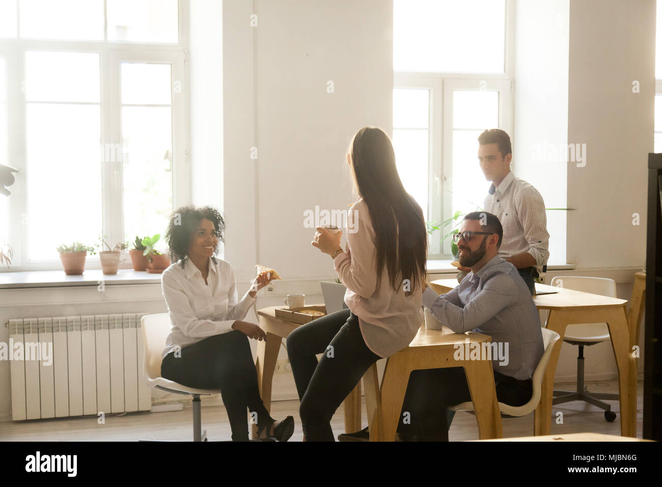 Smiling multiracial colleagues talking while eating pizza at off Stock ...