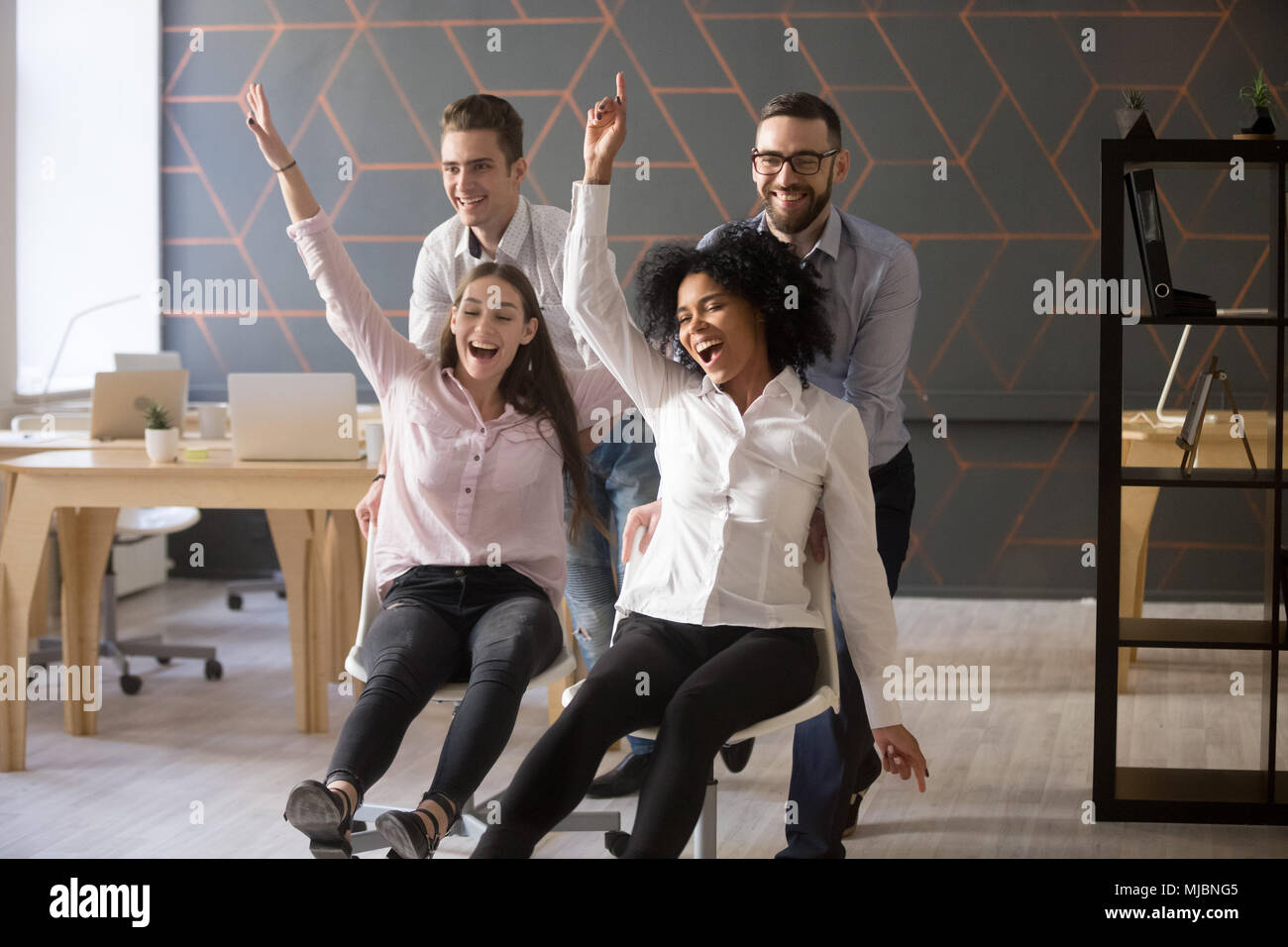 Excited diverse colleagues having fun riding oh chairs in office Stock ...