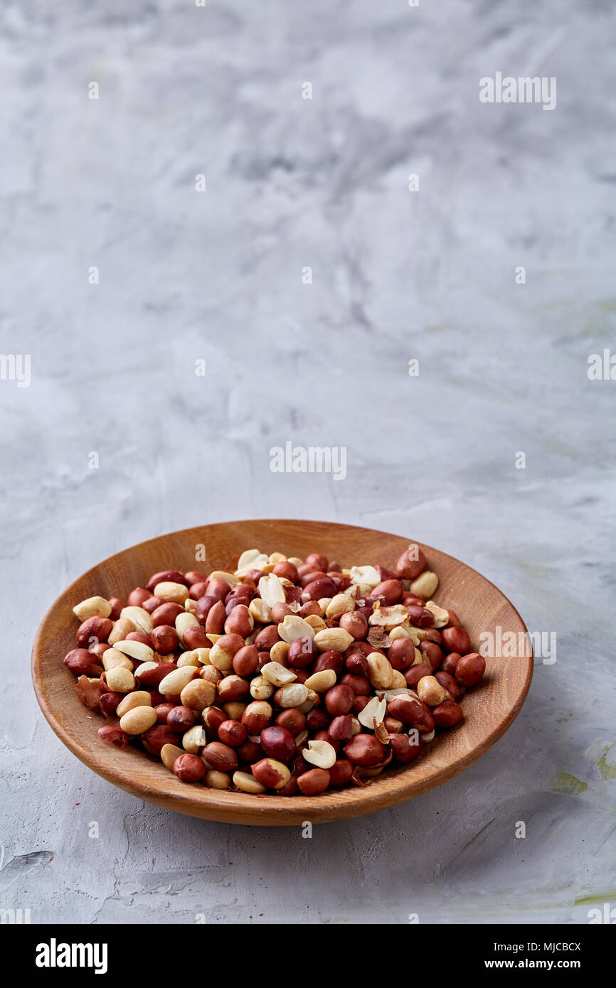 Mix of raw shelled peanuts in wooden plate isolated over white textured ...