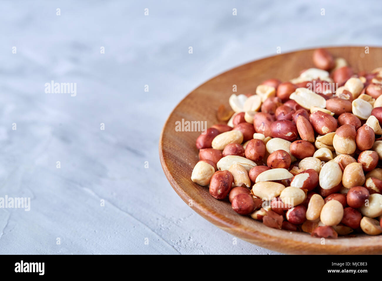 Mix of raw shelled peanuts in wooden plate isolated over white textured ...