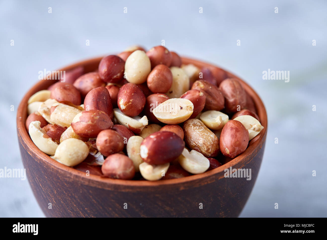 Mix of raw shelled peanuts in wooden plate isolated over white textured ...