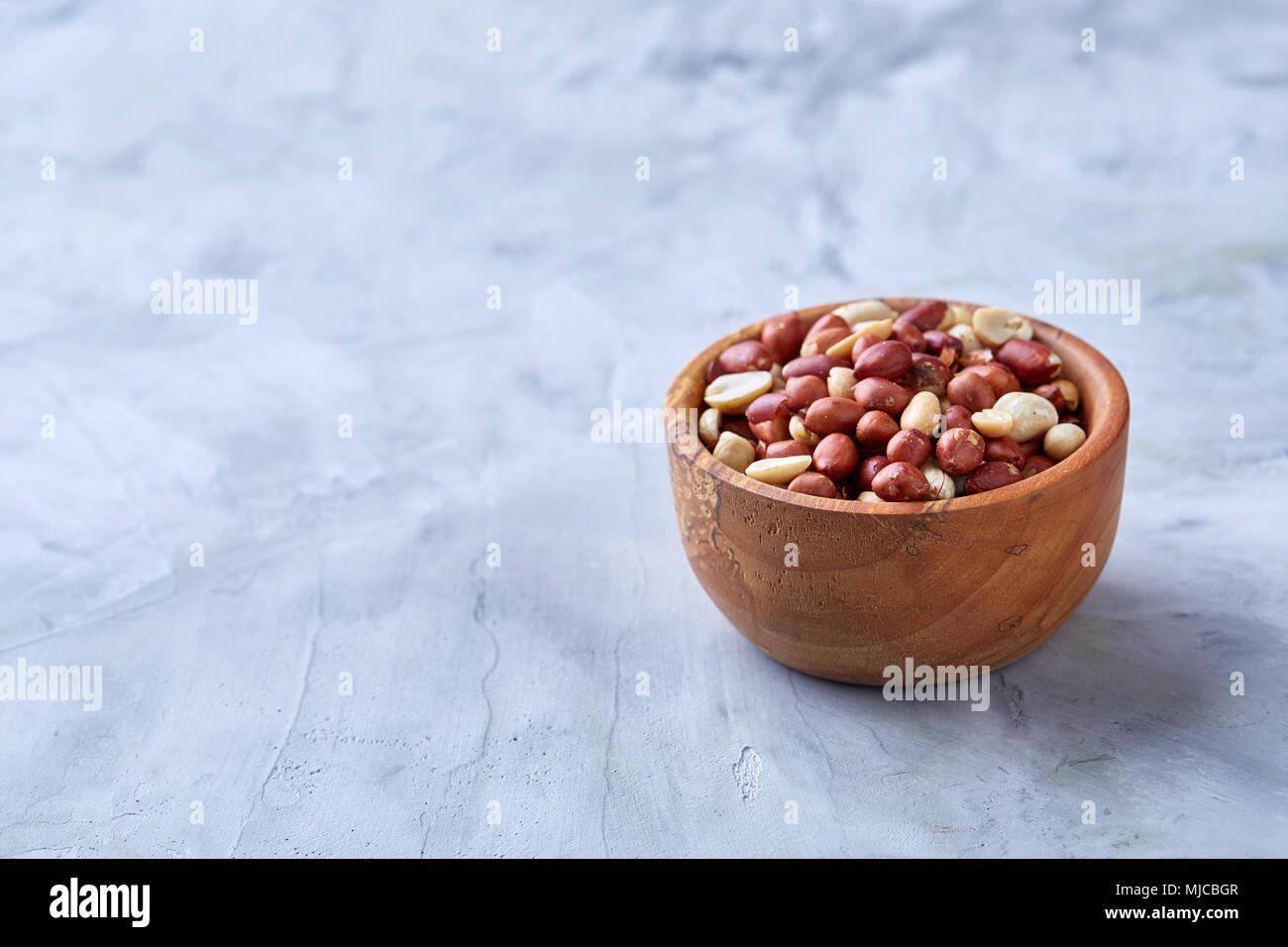 Mix of raw shelled peanuts in wooden plate isolated over white textured ...
