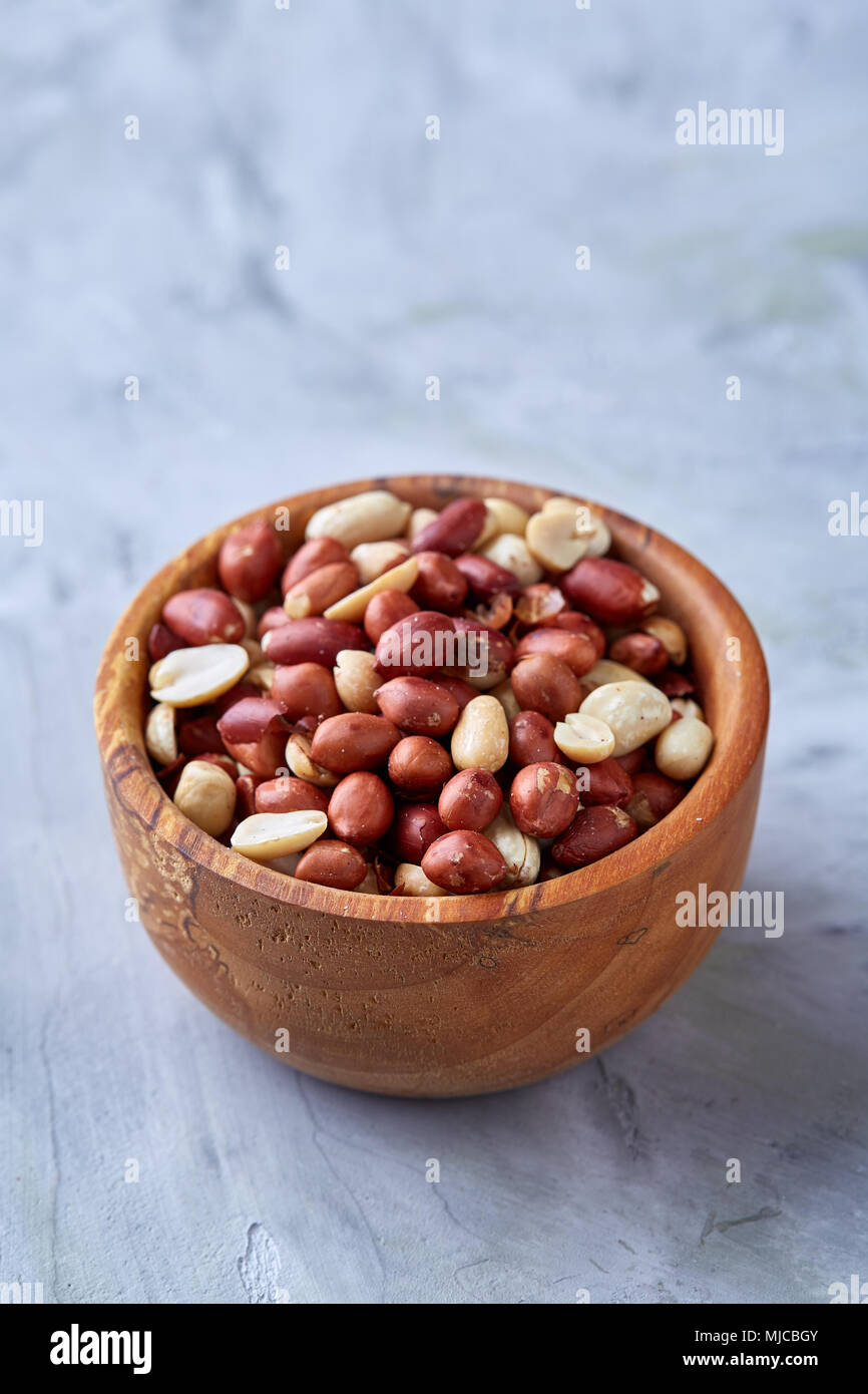 Mix of raw shelled peanuts in wooden plate isolated over white textured ...