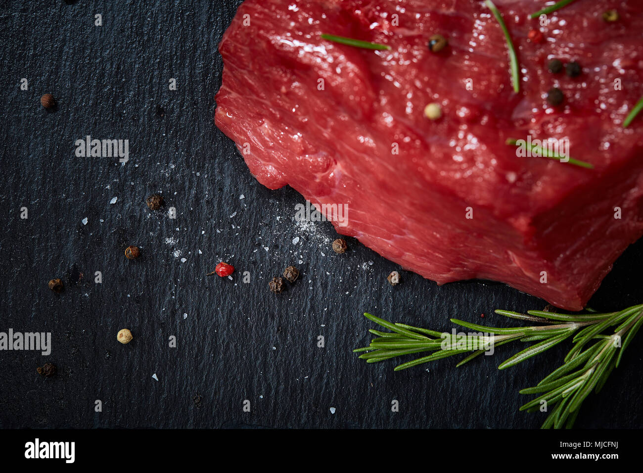 Raw meat beef steaks on black slate board with spices and rosemary over ...
