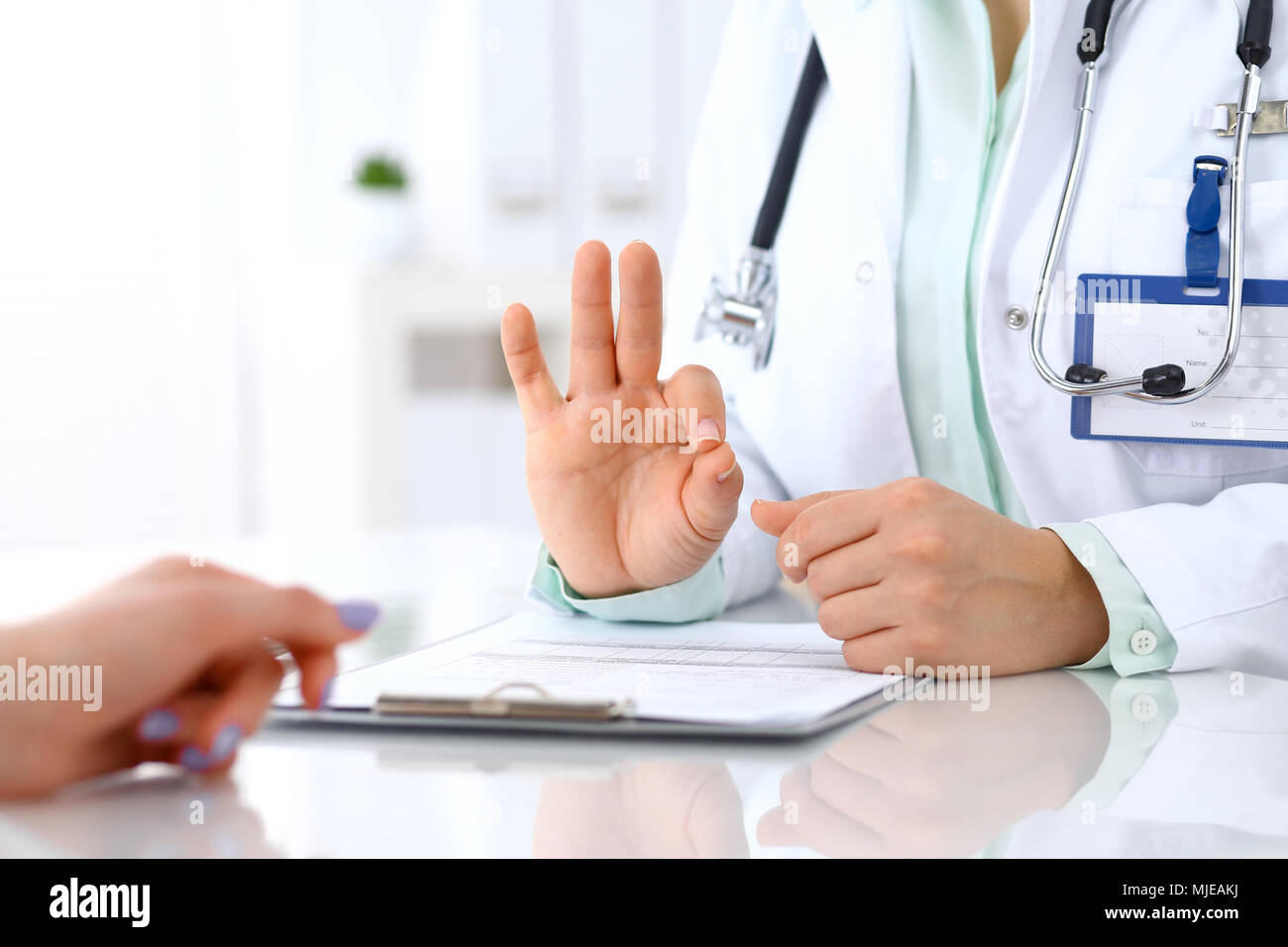 Doctor showing Ok sign to patient while sitting at the desk in hospital ...