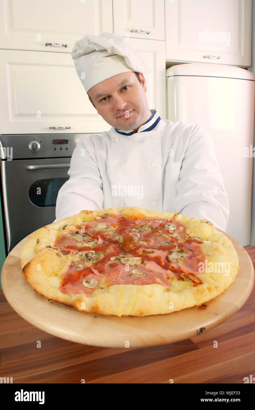 Pizza chef holding pizza on wooden plate and looks at you Stock Photo ...