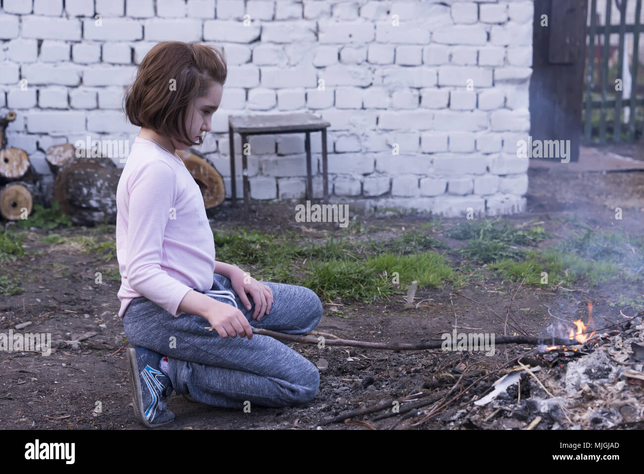 a little girl kindles a fire, crushes a stick of fire and firewood ...