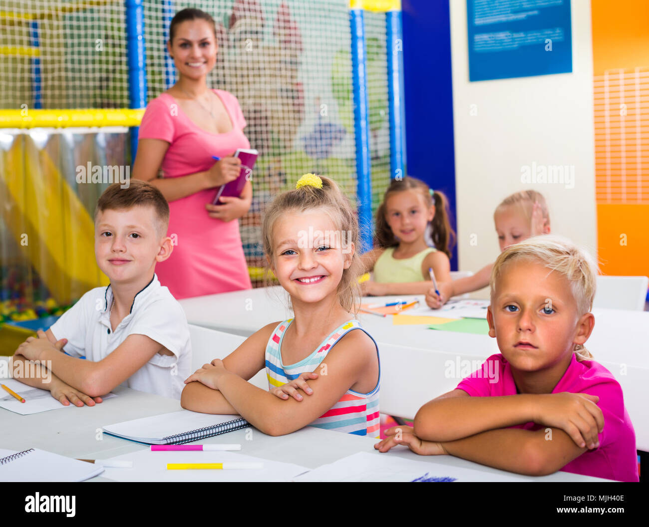 joyful smiling primary school kids sitting at school desks at lesson ...