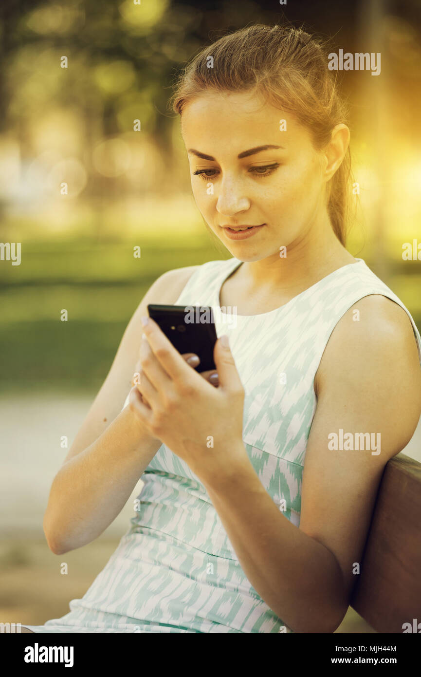 smiling british girl sitting on a bench and using telephone in outdoor ...