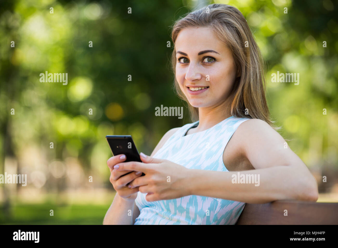 happy germany girl sitting on a bench and using phone in park Stock ...