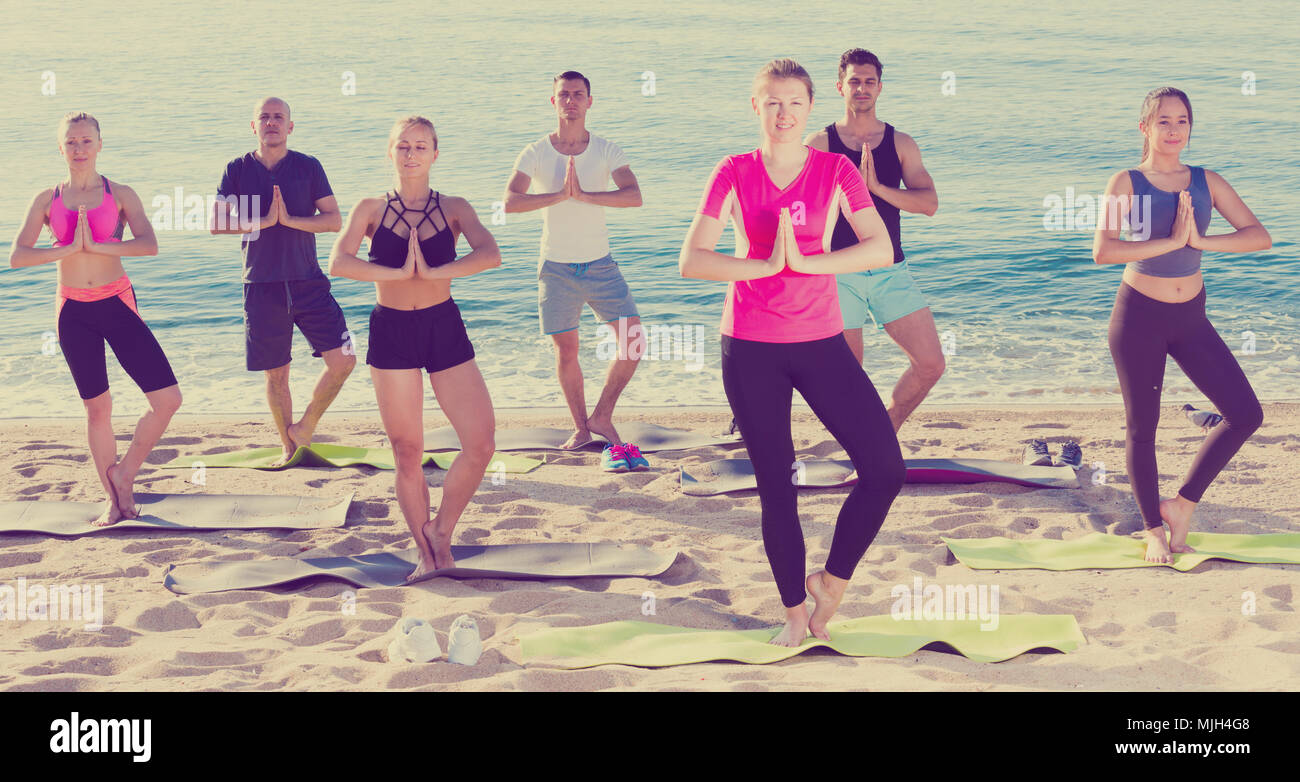 Young women and men exercising yoga poses on sunny beach by ocean Stock ...