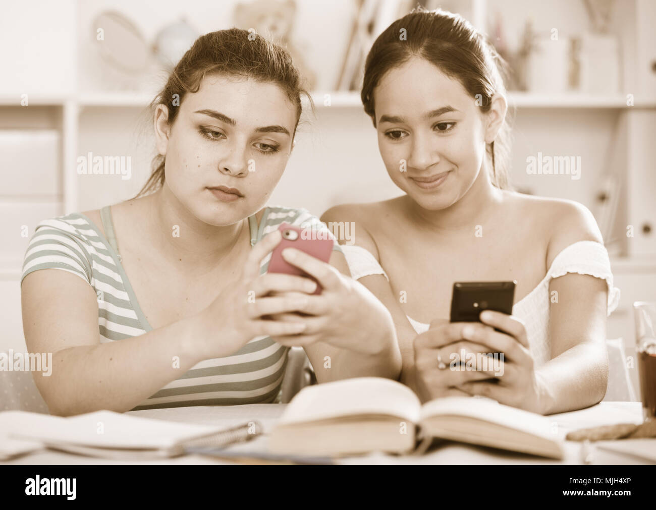 Cheerful teens girls spending time together at home, chatting on phones ...