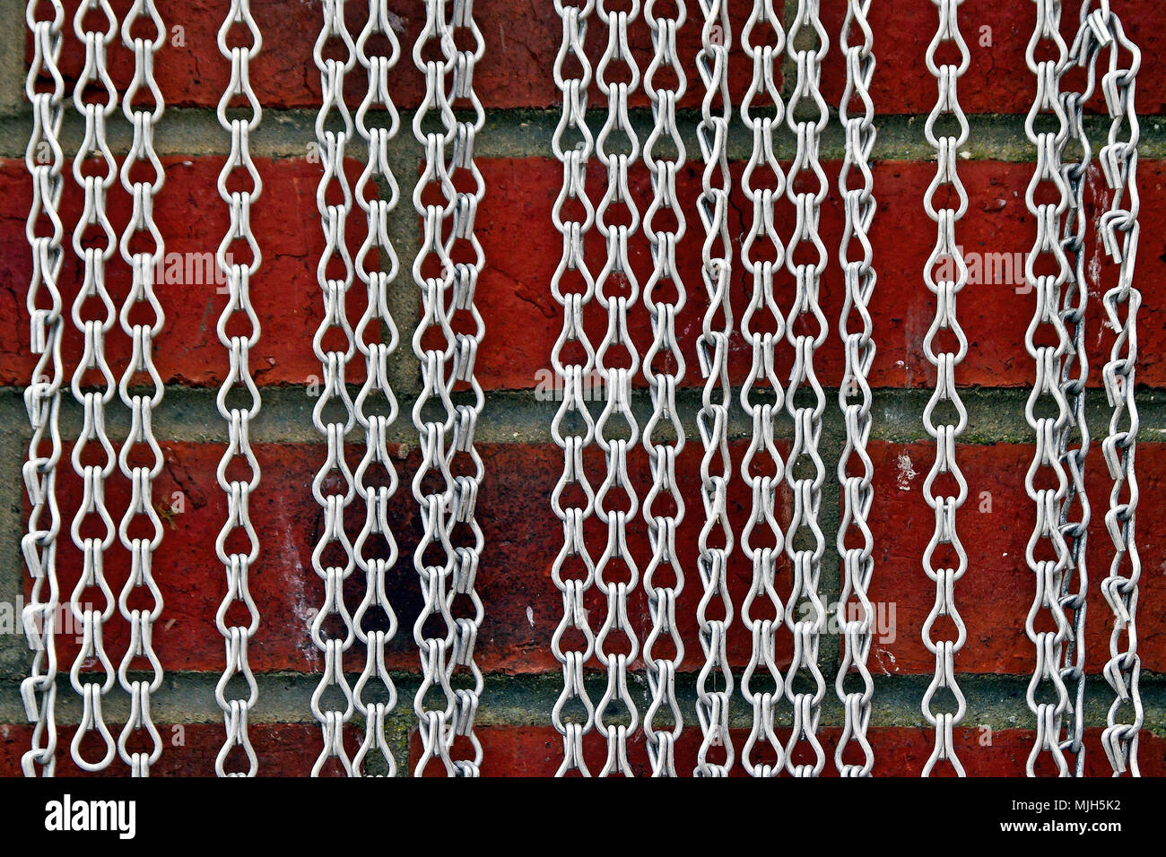 Strands of chains form a linear pattern against red brickwork on ...