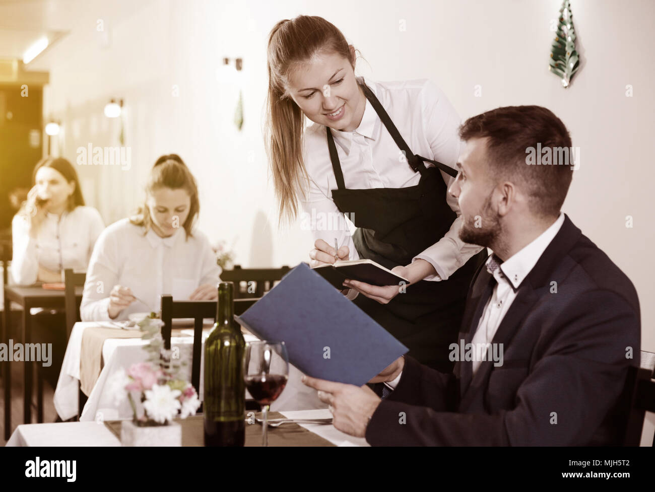 Welcoming female waiter is taking order from businessman in restaurante ...