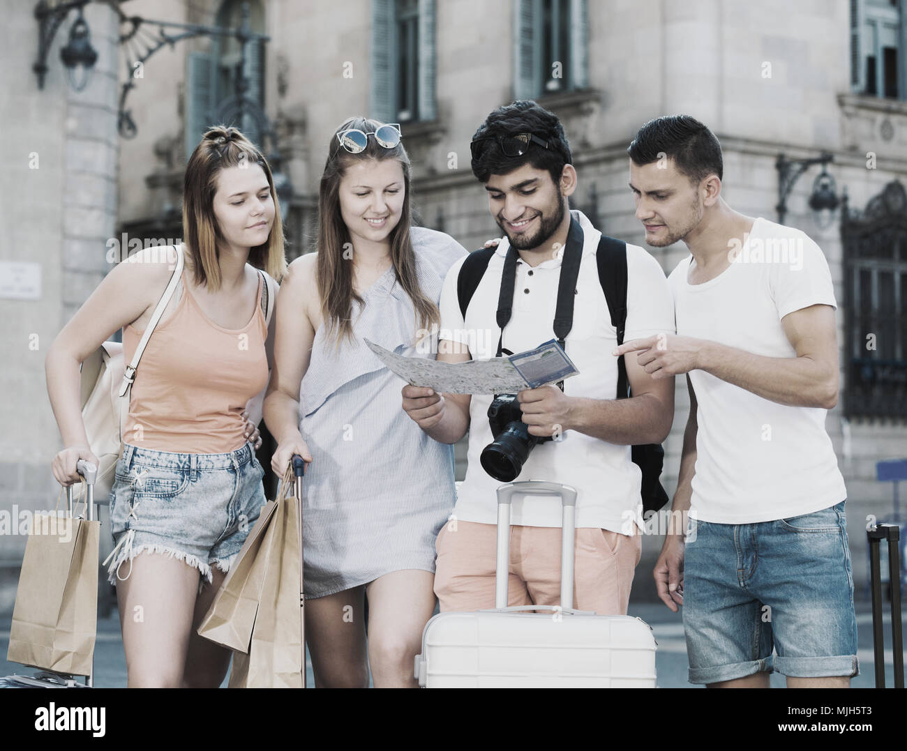 Four cheerful traveling young people searching for direction using ...