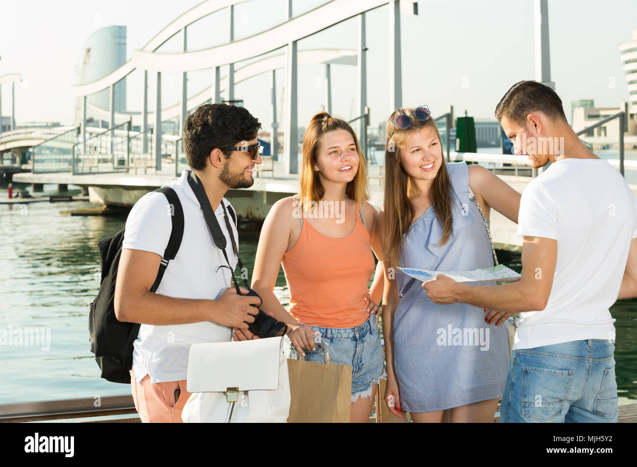 Four smiling traveling young people searching for direction using paper ...