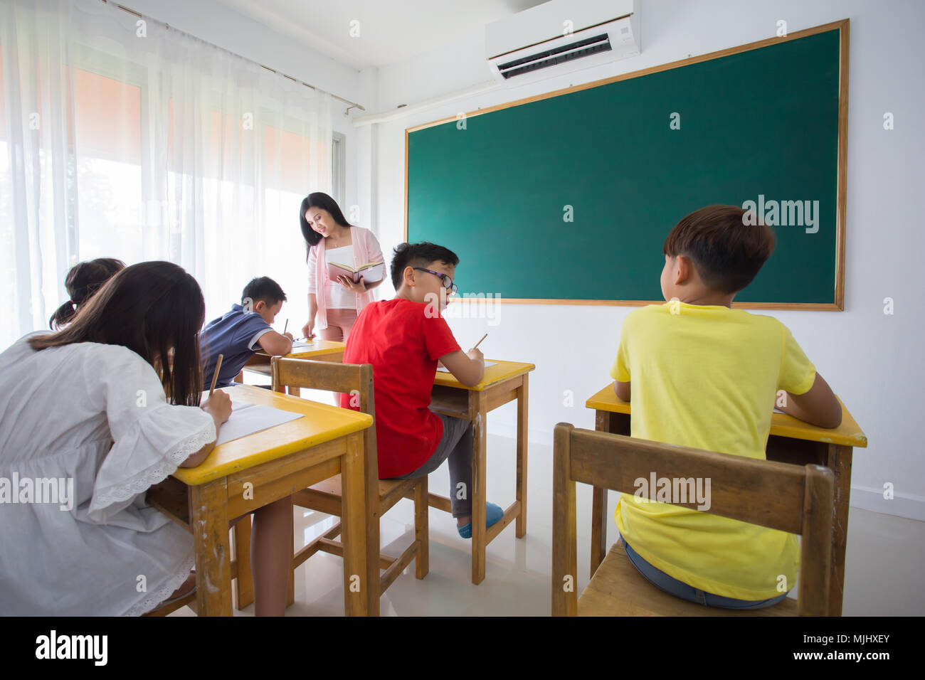 Group of school kids with pens and notebooks studying in classroom with ...