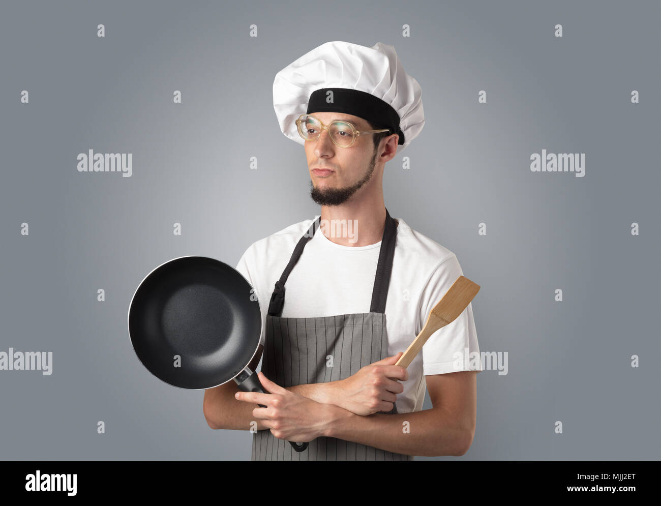 Young bearded cook portrait with kitchen tools and empty wallpaper ...