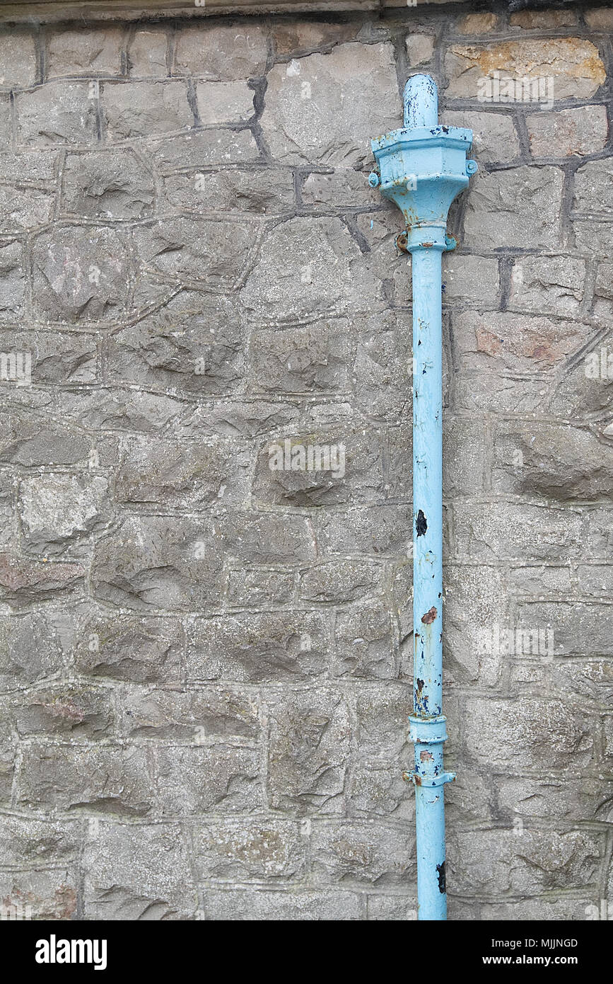 Old blue metal drainpipe with flaky paint on a grey stone wall ...